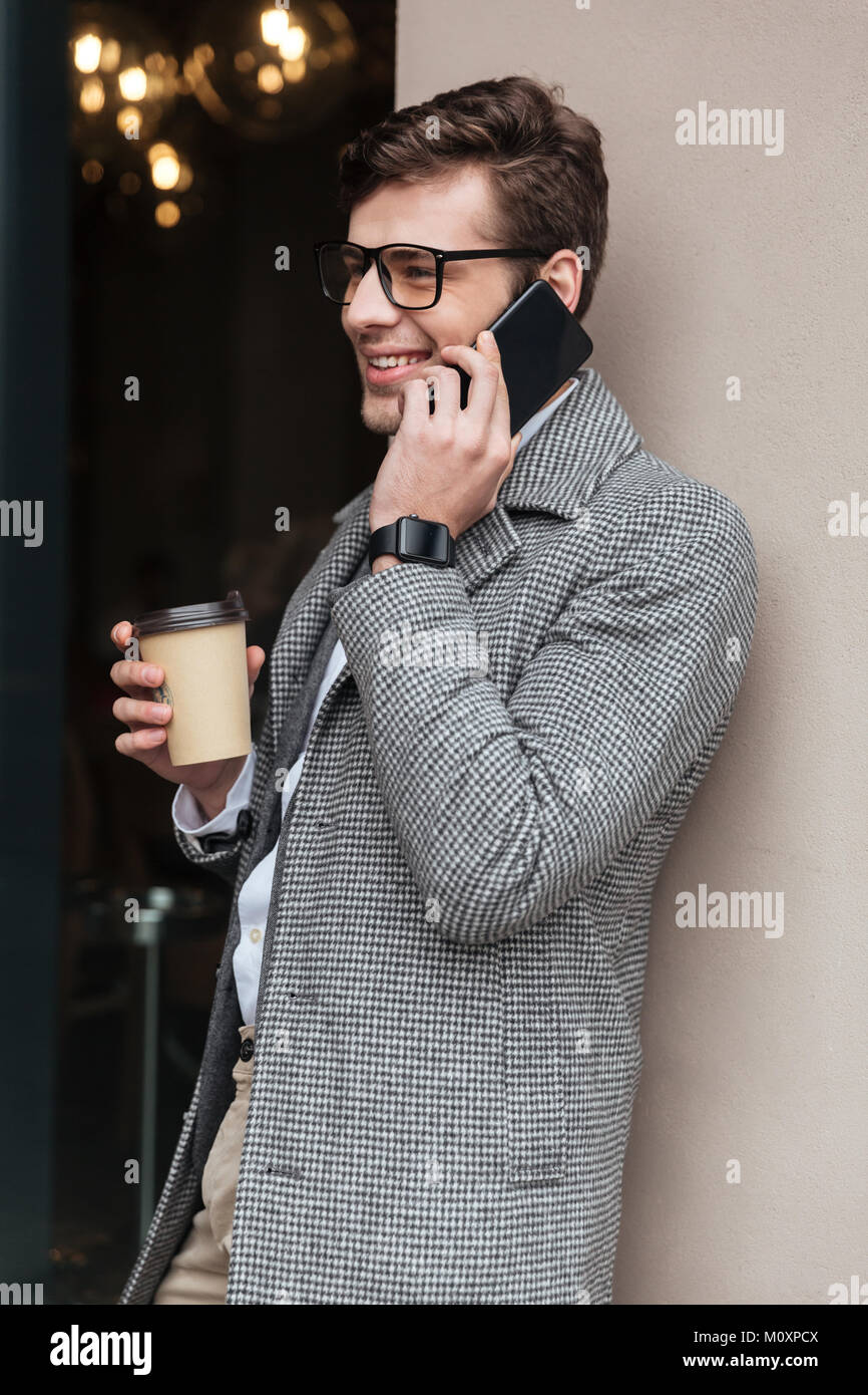 Vertical image of smiling business man in eyeglasses and coat talking ...