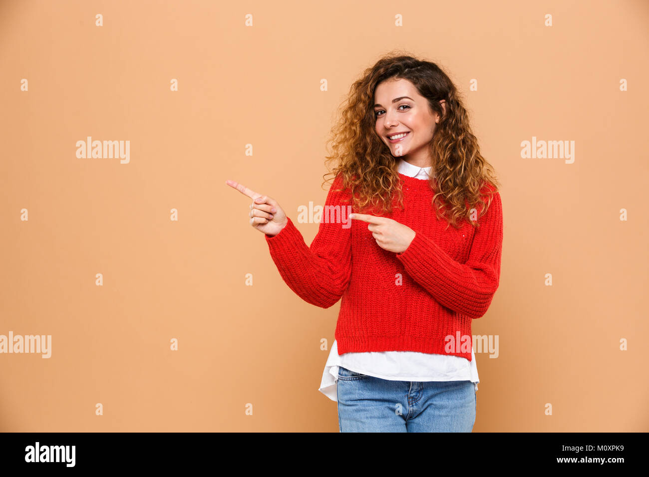 Portrait of a happy pretty girl standing and pointing two fingers away ...