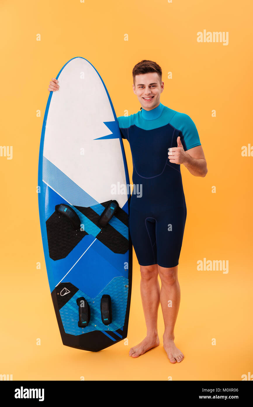 Full length photo of handsome surfer guy in suimsuit holding surfboard ...