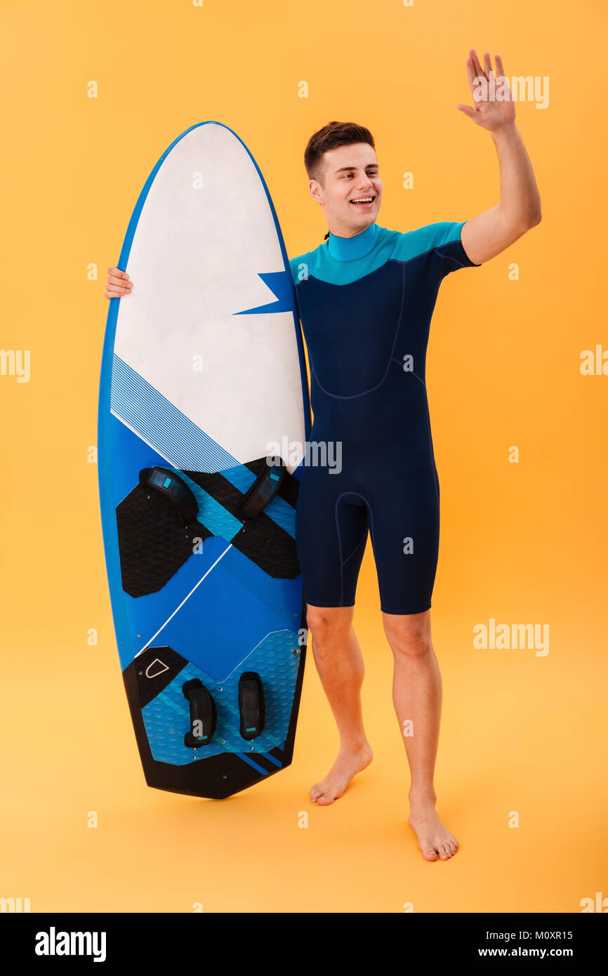 Full length photo of young surfer guy with surfboard showing greeting ...