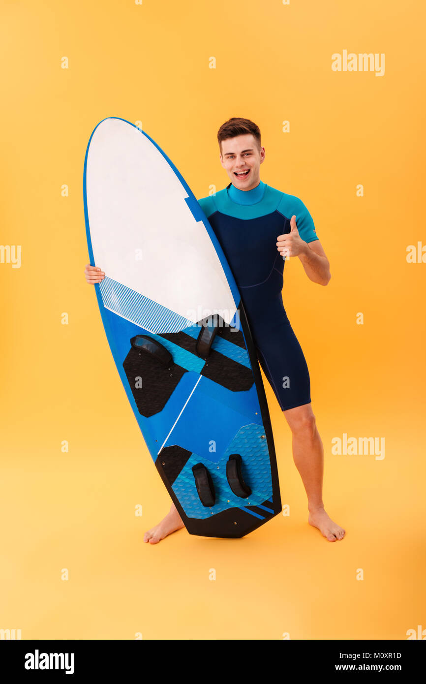 Full length portrait of happy handsome surfer showing thumb up gesture ...