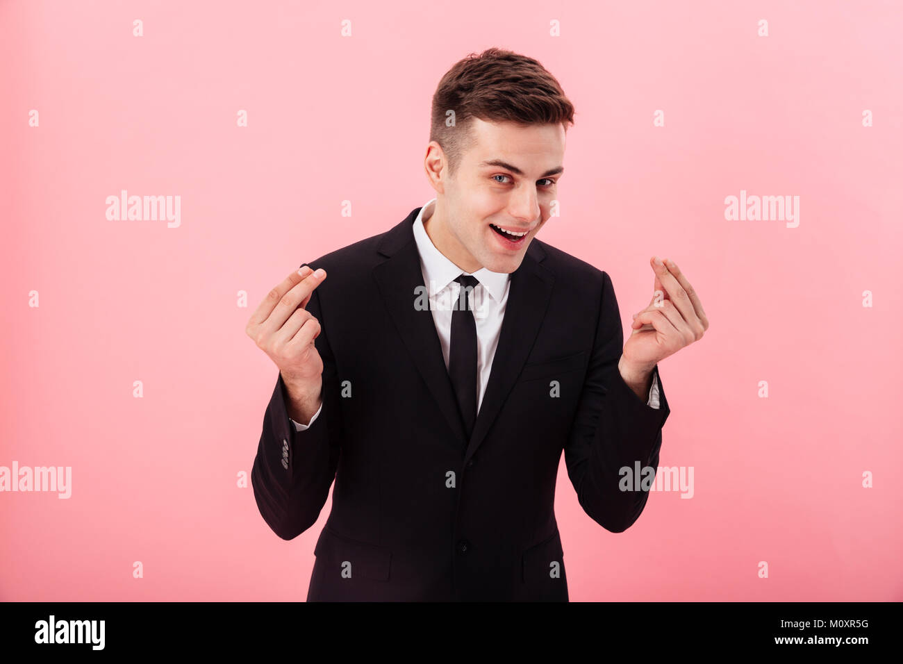 Young funny man in suit showing money gesture and smiling to camera ...