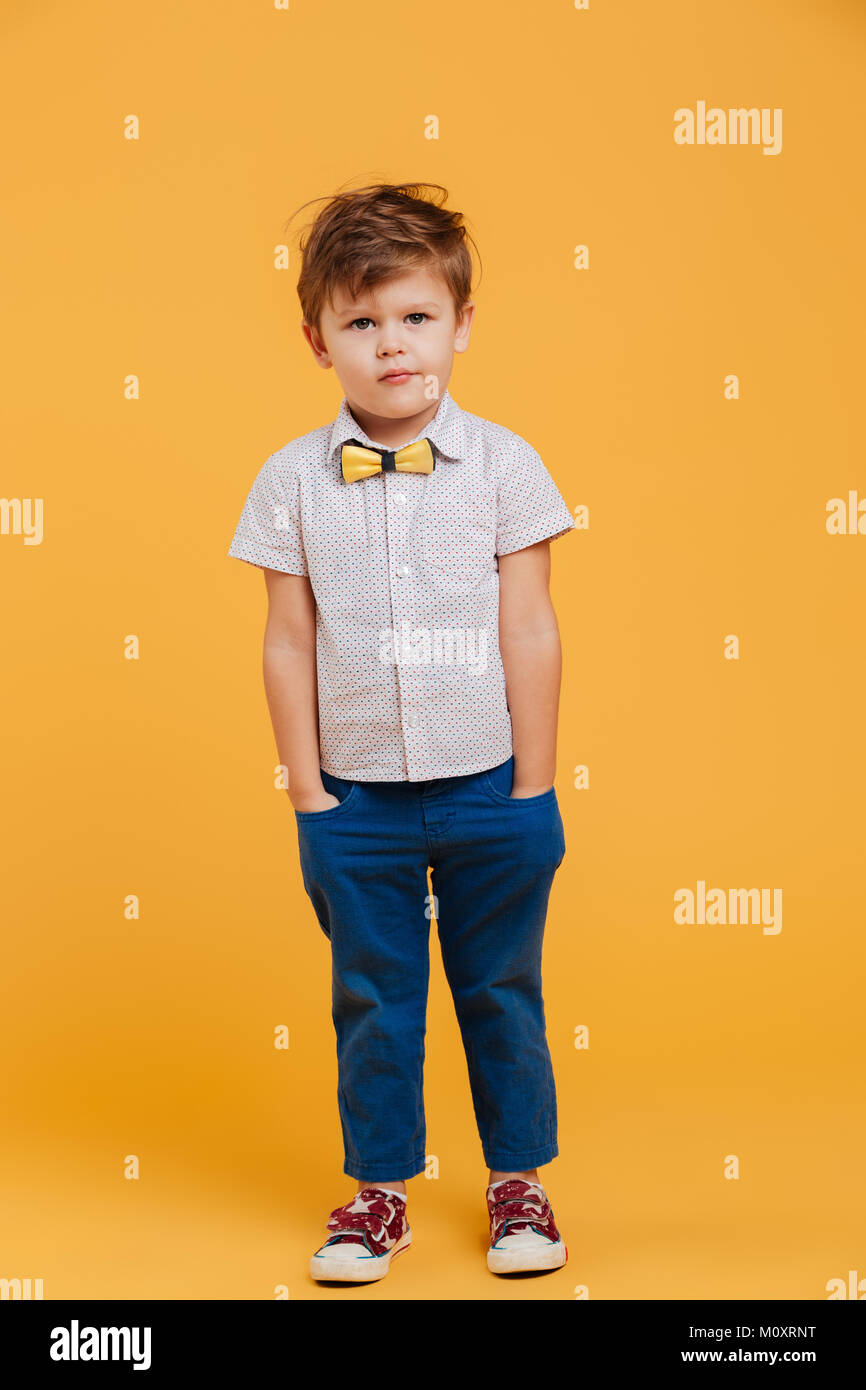 Photo of serious little boy child standing isolated over yellow ...