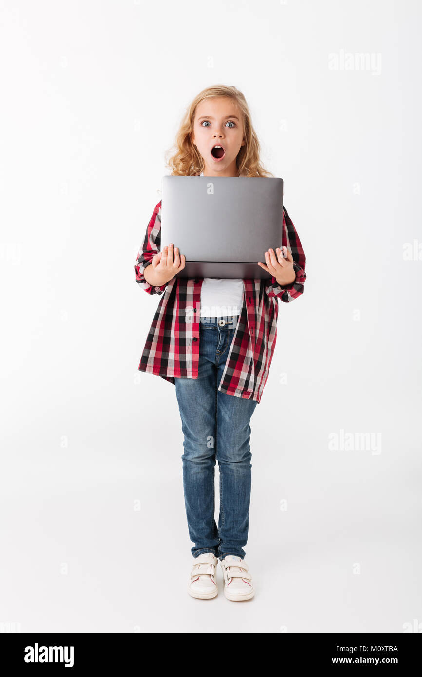 Full length portrait of a shocked little girl holding laptop computer ...