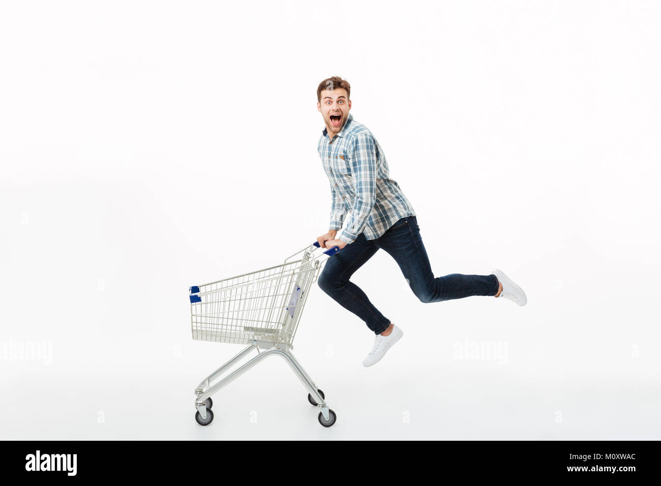 Full length portrait of a cheerful man jumping with a shopping trolley ...