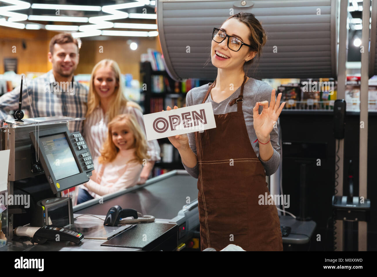 Portrait of smiling woman cashier holding open sign and showing ok ...