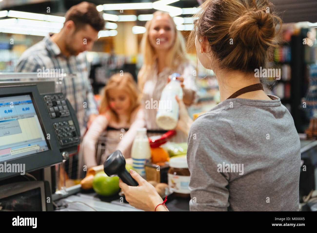 Cheerful family standing at the cash counter buying groceries at the ...