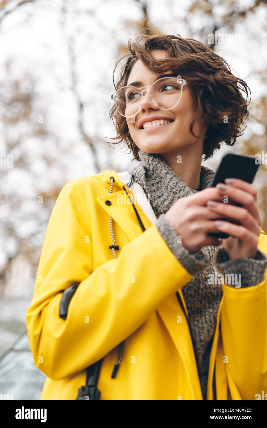 Smiling nice woman in yellow raincoat typing text message or scrolling ...