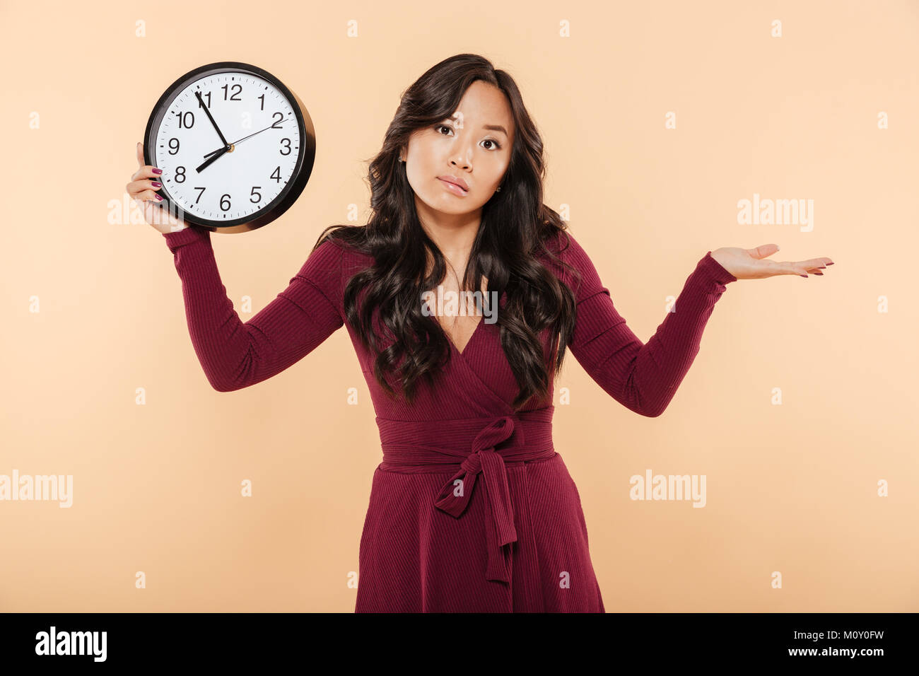 Cute brunette woman with curly long hair holding clock showing nearly 8 ...