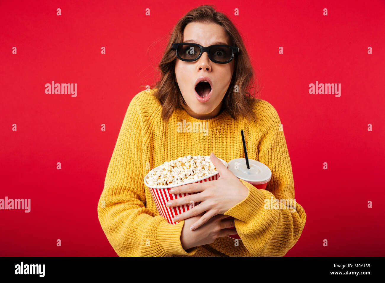 Portrait of a shocked woman in sunglasses holding popcorn and plastic ...