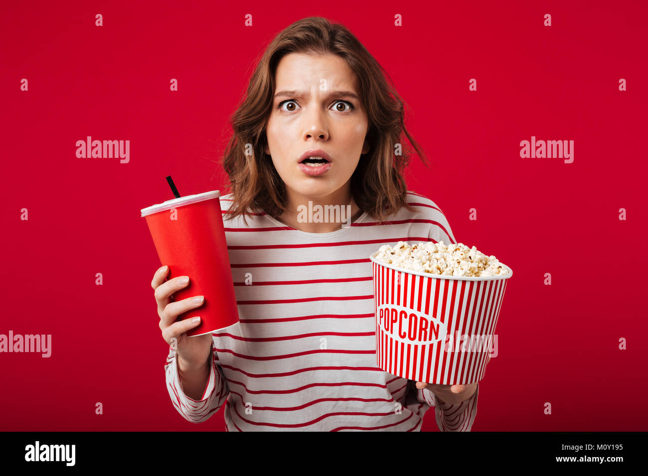 Portrait of a shocked woman holding popcorn and plastic cup isolated ...