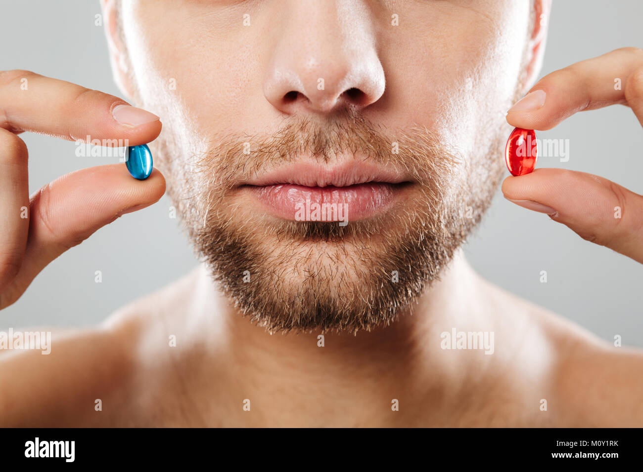 Close up portrait of a serious man holding two capsules at his face ...