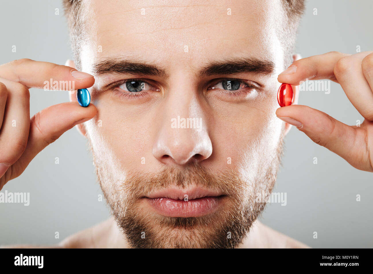 Portrait of a confident man holding two capsules at his face isolated ...