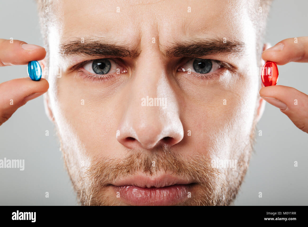 Portrait of a serious man holding two capsules at his face isolated ...