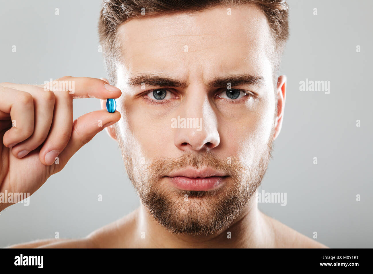 Portrait of a bearded man holding blue capsule at his face isolated ...