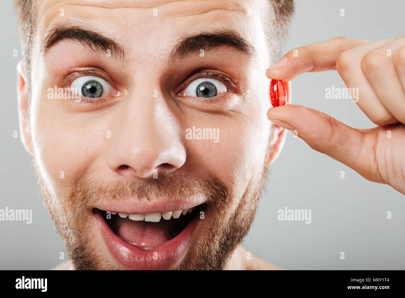 Close up portrait of a happy man holding red capsule at his face ...