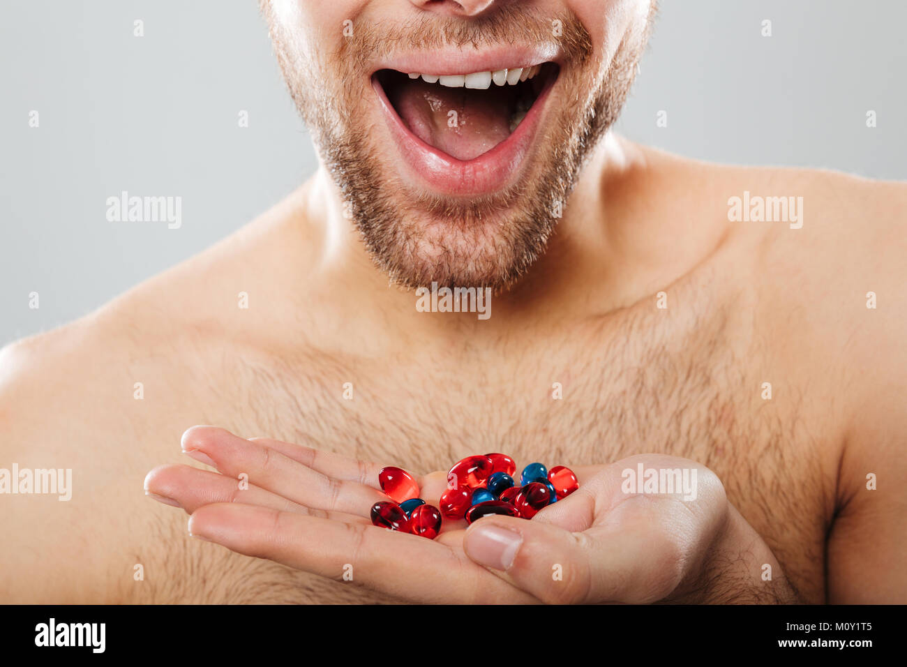Cropped image of a happy man holding red and blue capsules on his palm ...