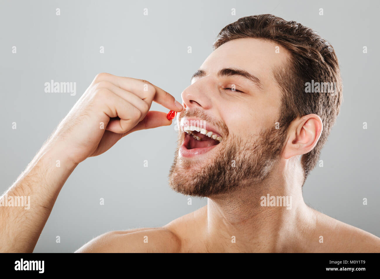 Portrait of a happy man taking a red capsule isolated over gray ...