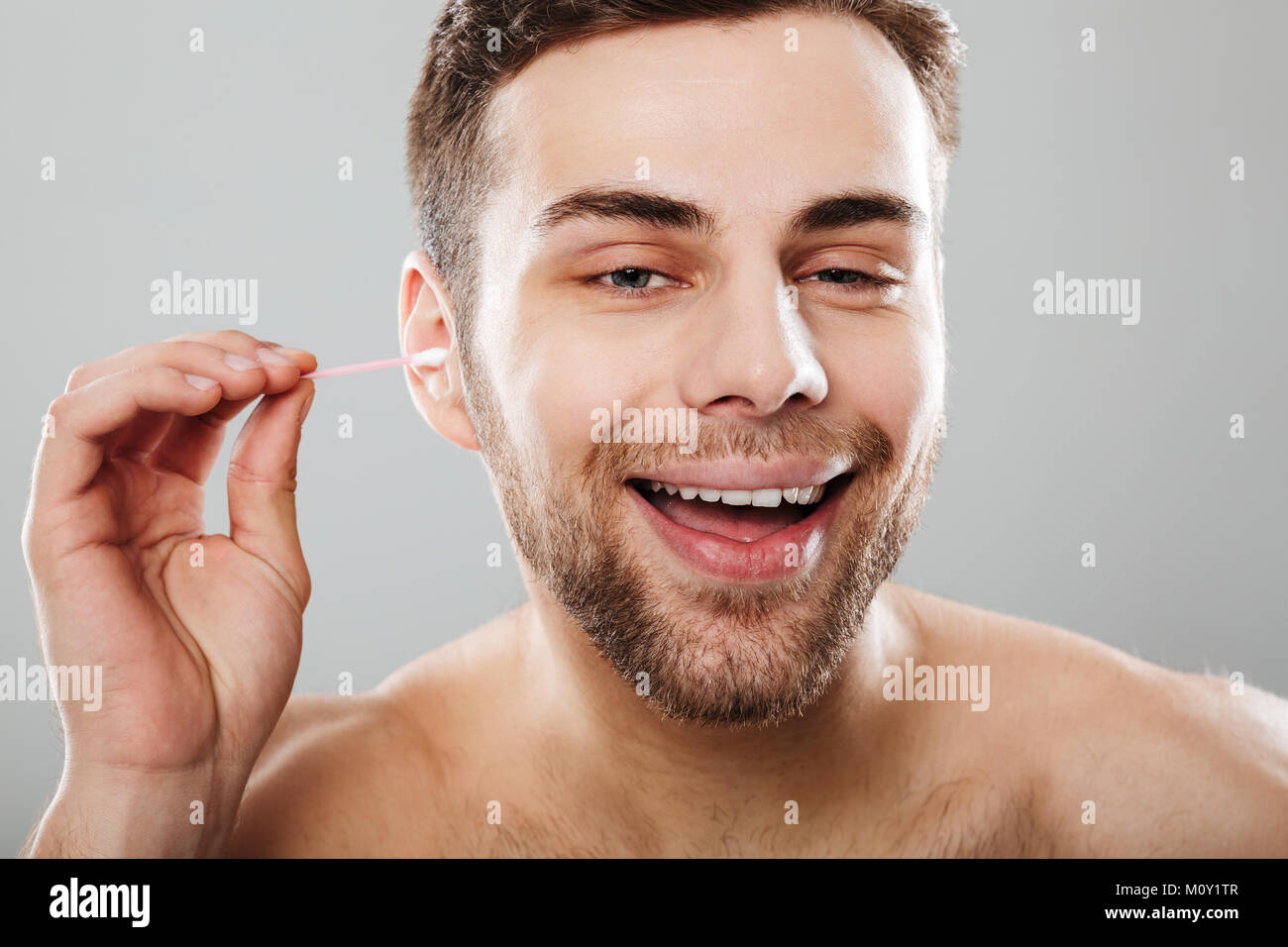 Close up portrait of a smiling man cleaning his ears with a cotton swab ...