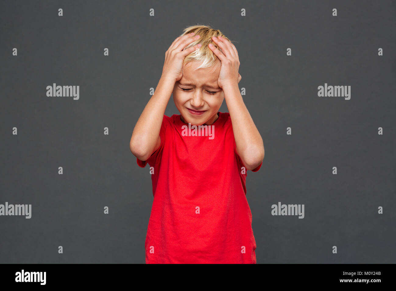 Photo of sad little boy child with headache standing isolated over grey ...