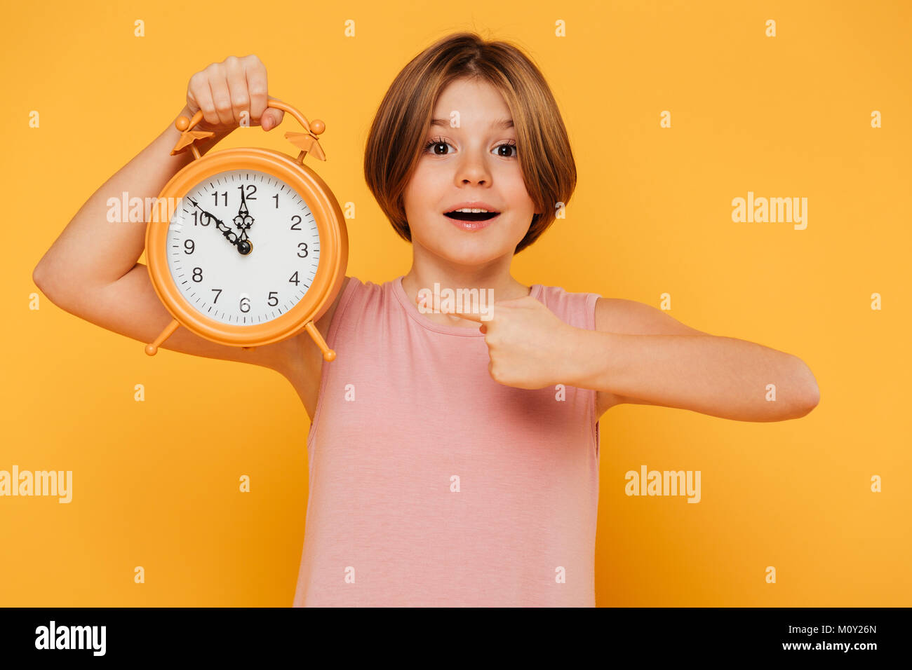 Happy little girl pointing with finger at alarm clock while looking ...
