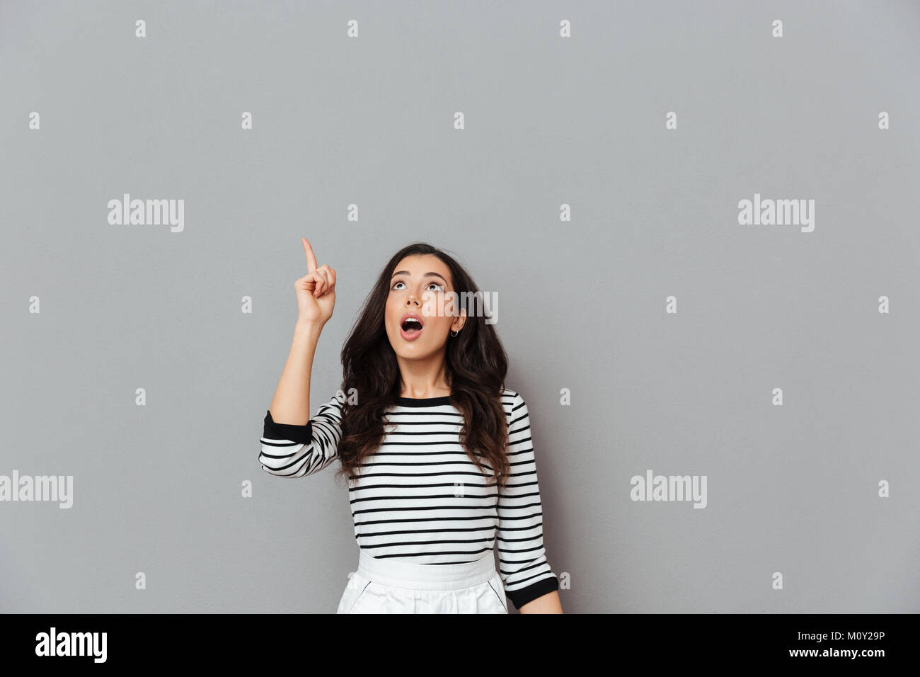 Portrait of a shocked woman pointing finger up at copy space isolated ...