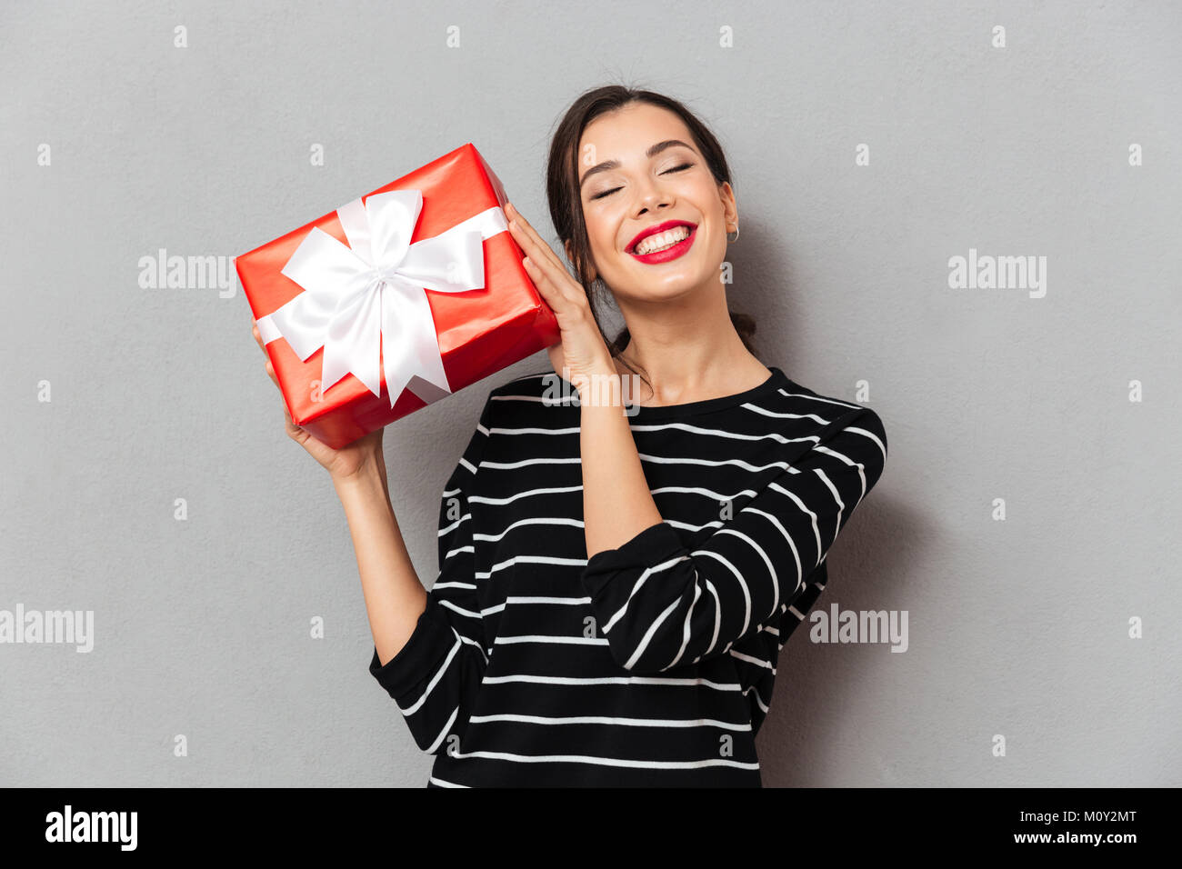 Portrait of a delighted woman holding gift box while standing with eyes ...