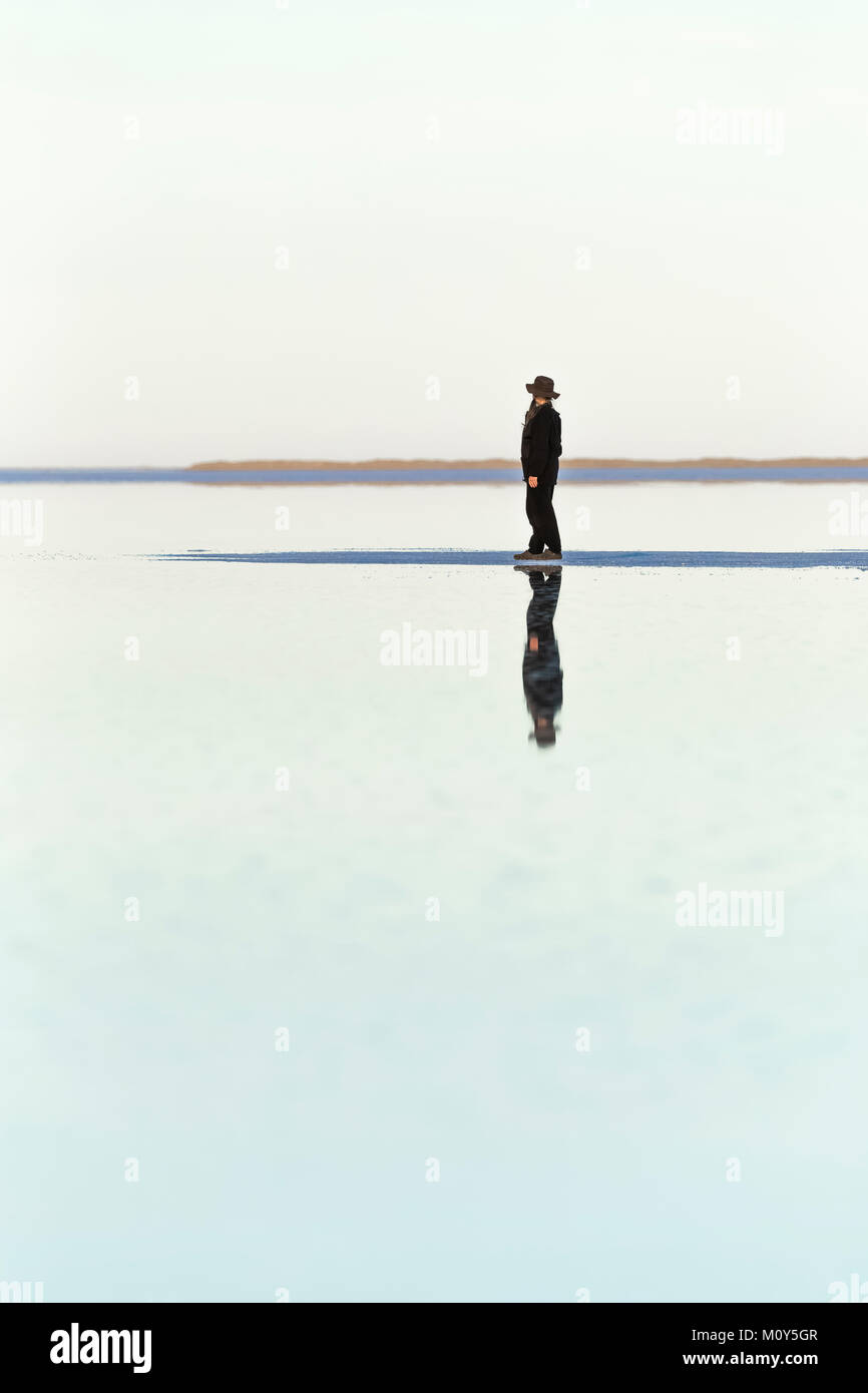 Woman walking on a spit of land extending out into shallow salt water ...