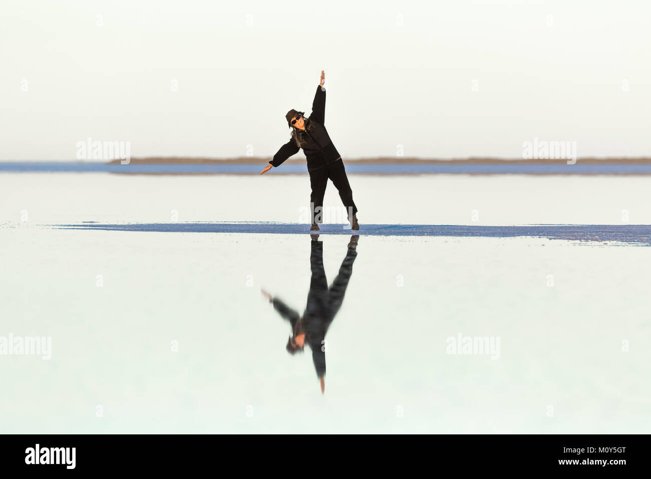 Woman walking on a spit of land extending out into shallow salt water ...