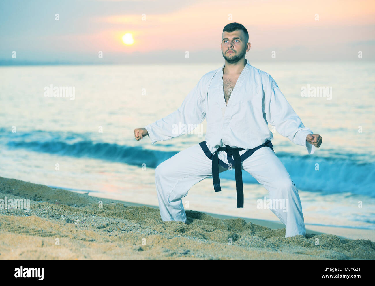 Concentrated active guy doing karate poses at sunset sea shore Stock ...