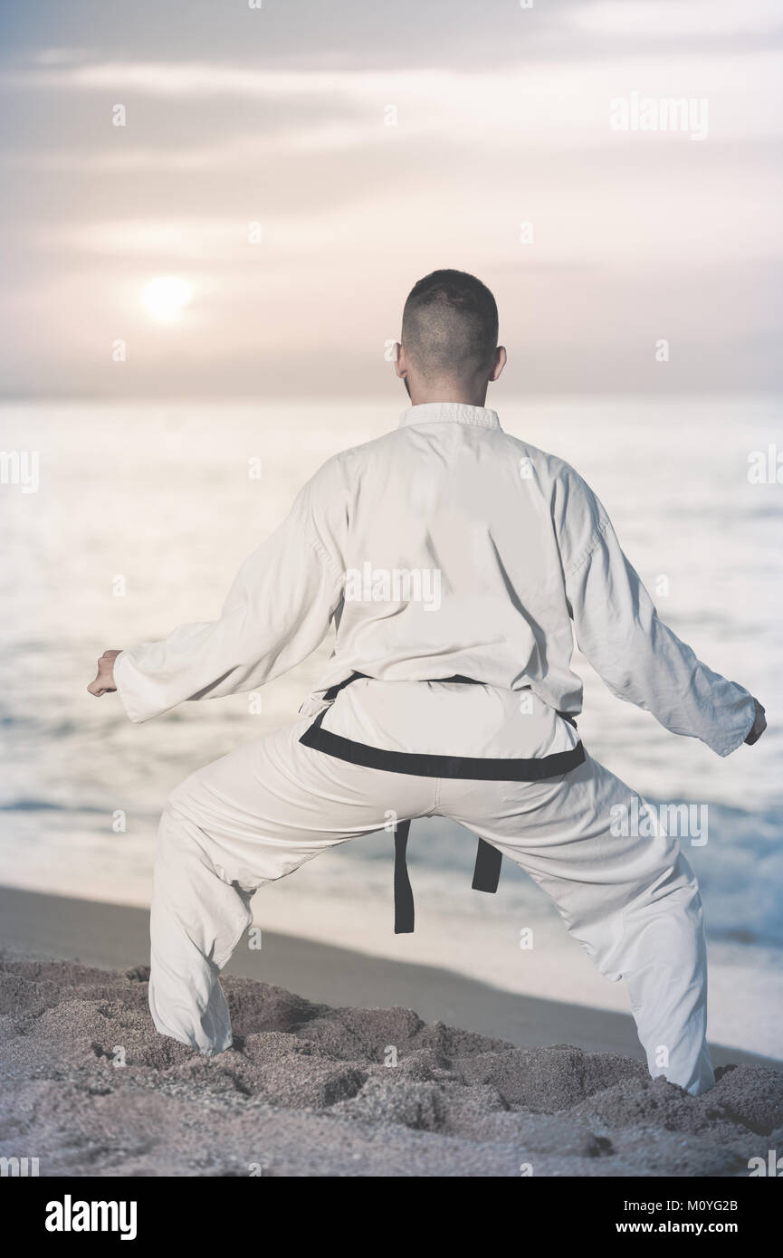 Young male is training the Shiko-dachi stance on the beach near the sea ...