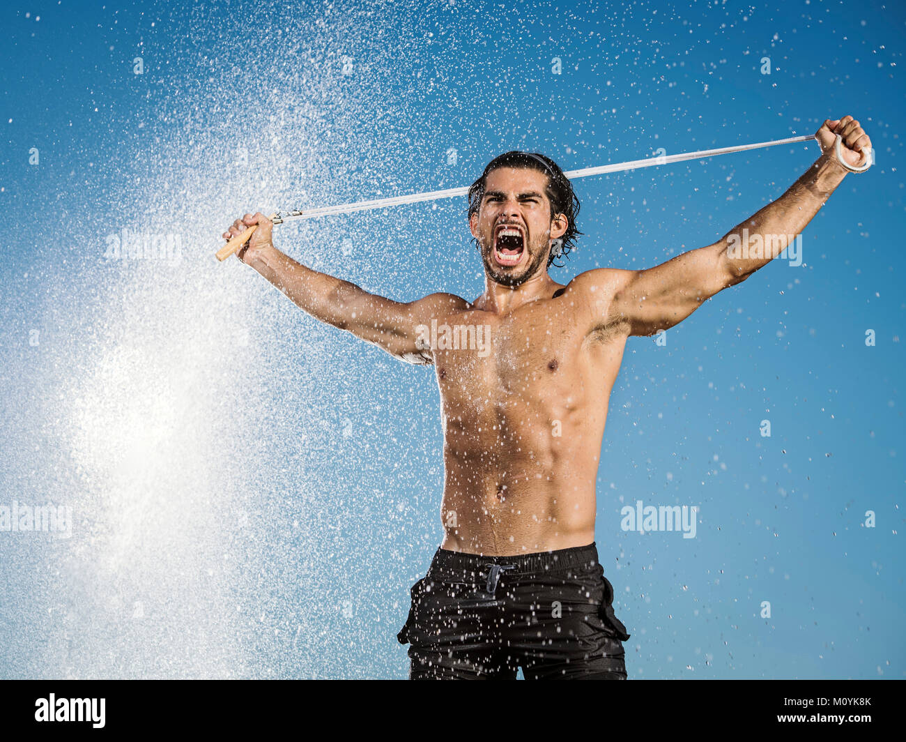 Water spraying on Hispanic man holding jump rope Stock Photo - Alamy