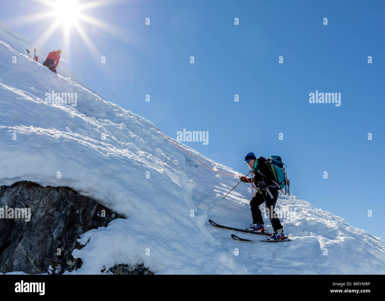 Alpine ski mountaineers belayed on rope to ski steep downhill slope ...