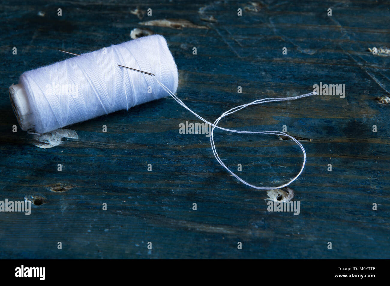 White thread and sewing needle on rustic blue background with space for ...