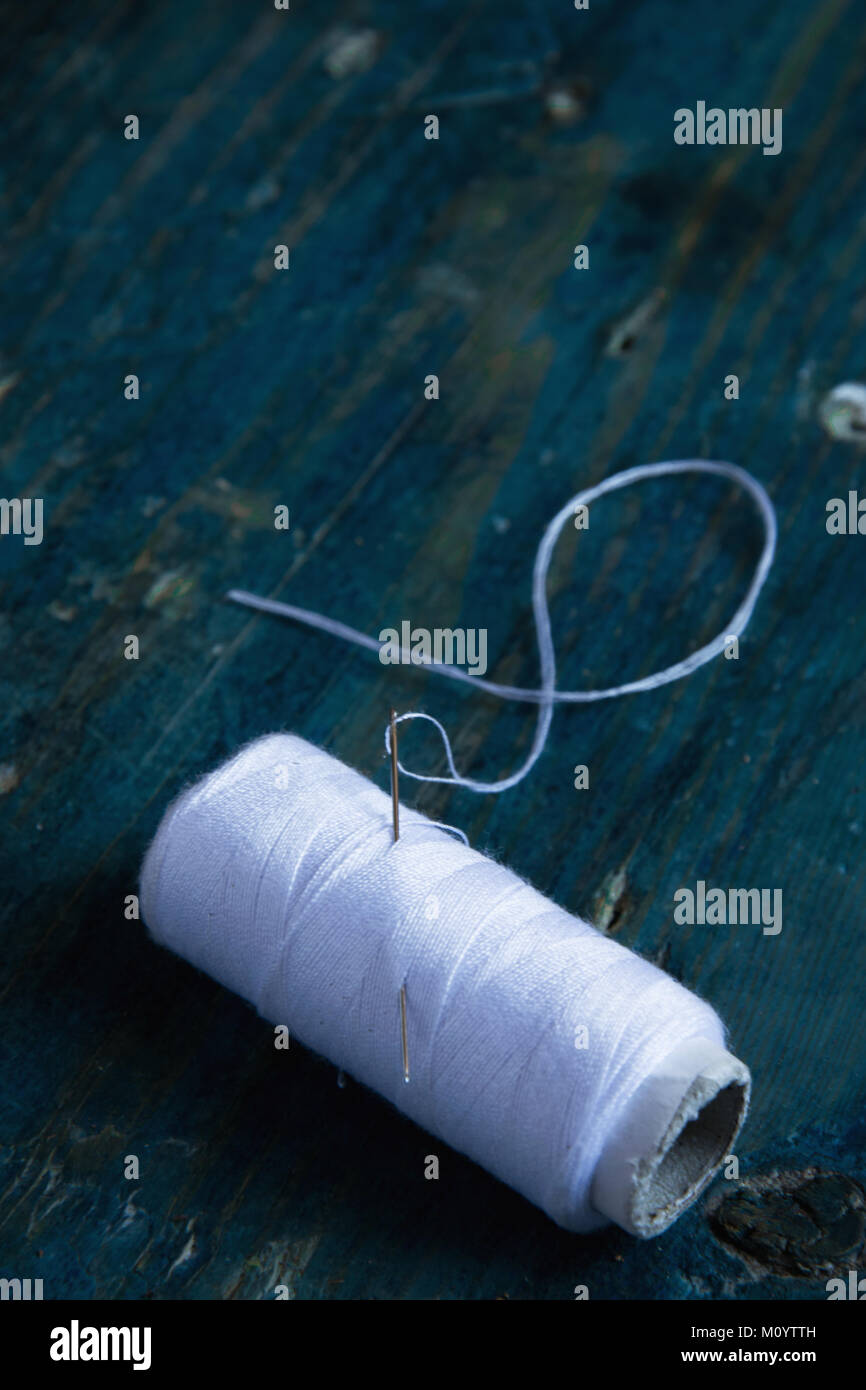 White thread and sewing needle on rustic blue background with space for ...