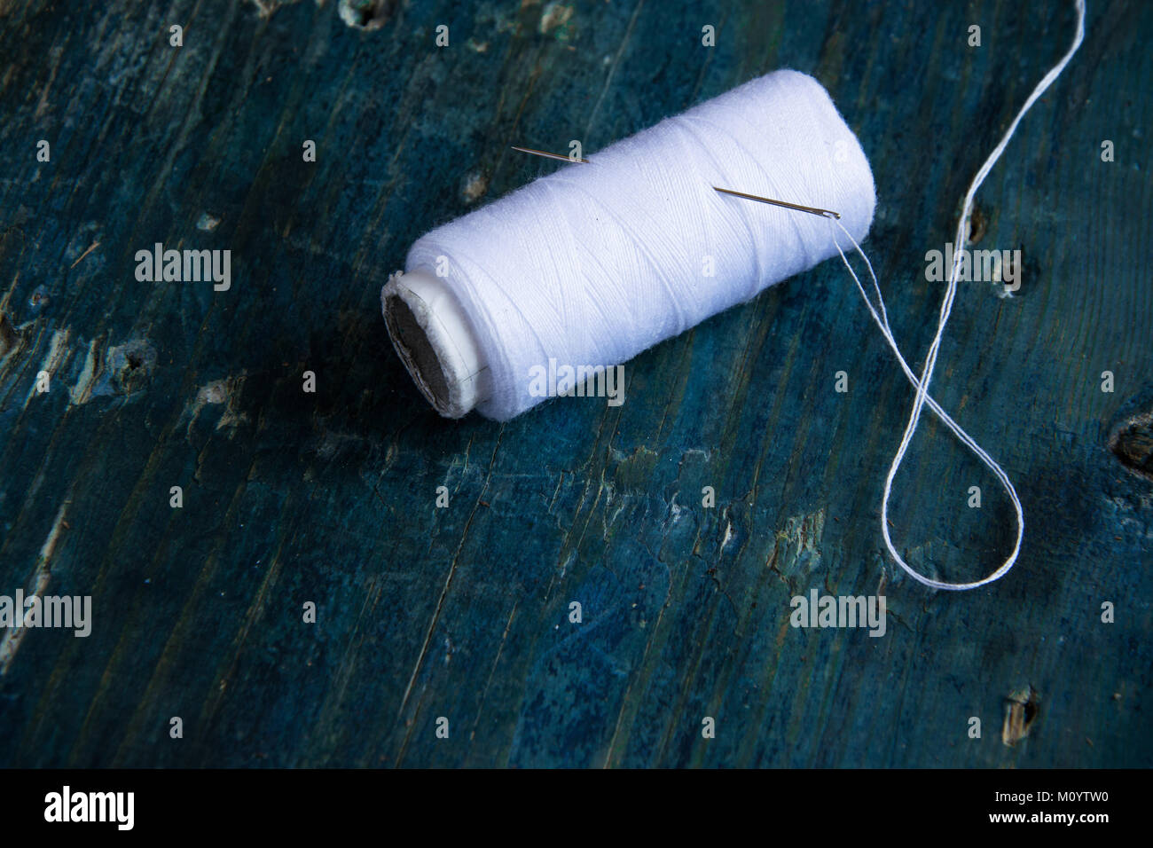 White thread and sewing needle on rustic blue background with space for ...