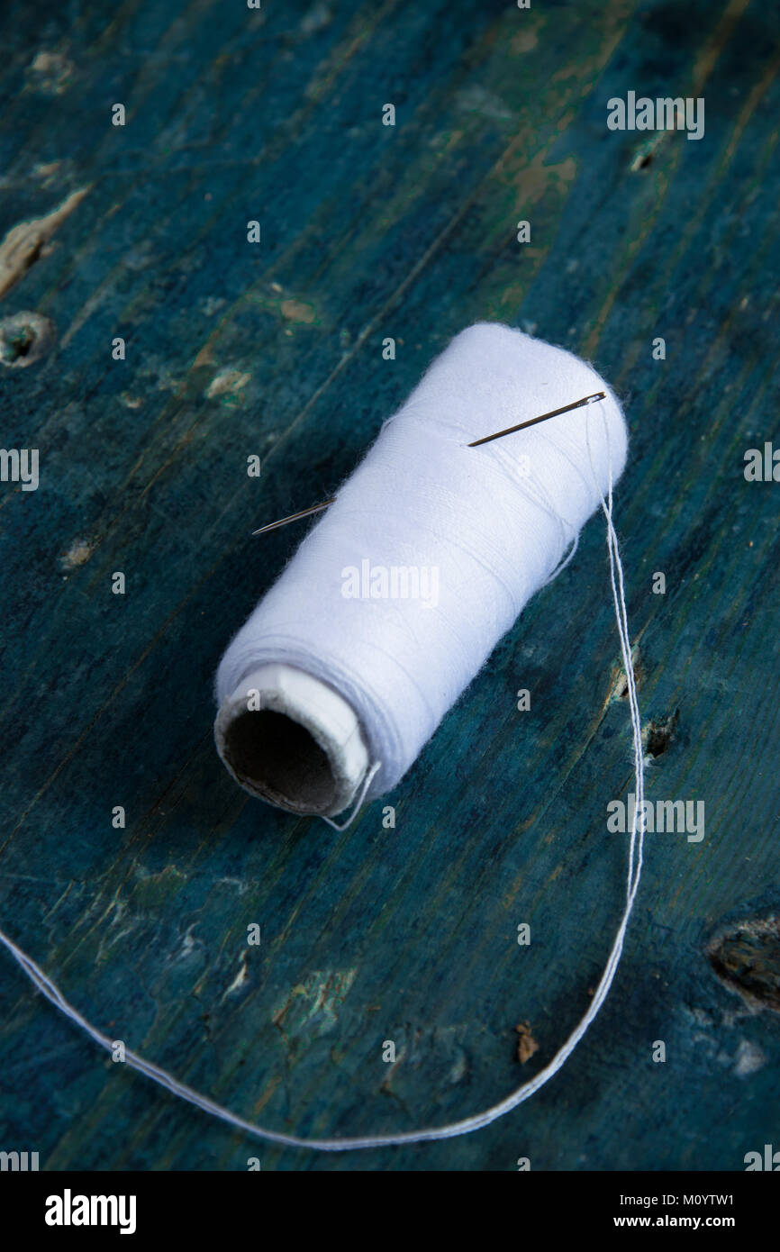 White thread and sewing needle on rustic blue background with space for ...