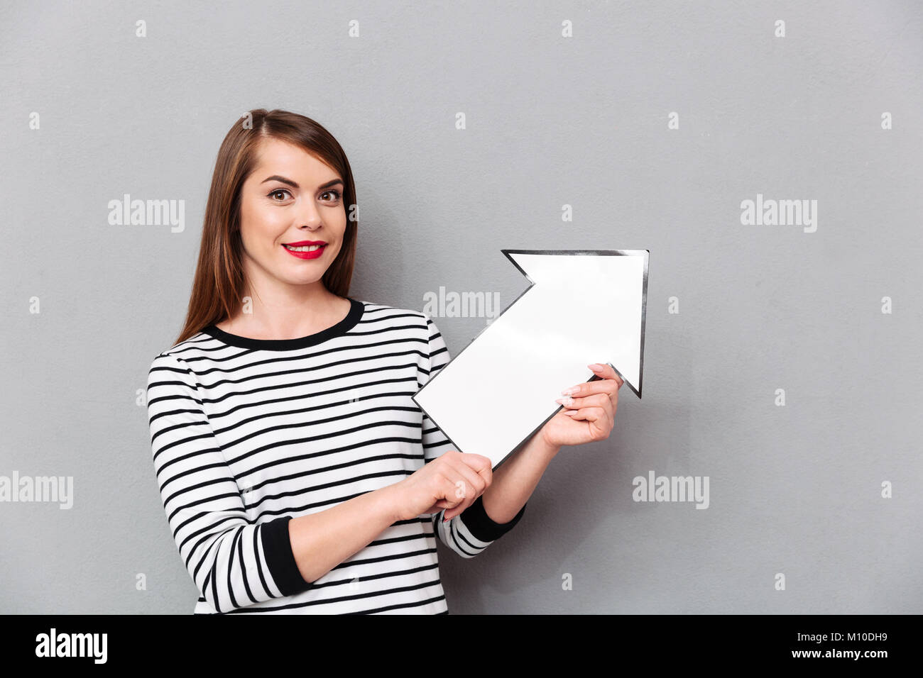 Portrait of a smiling woman pointing paper arrow up at copy space ...
