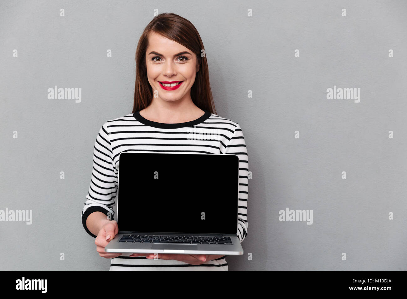 Portrait of a cheerful woman showing blank screen laptop computer while ...