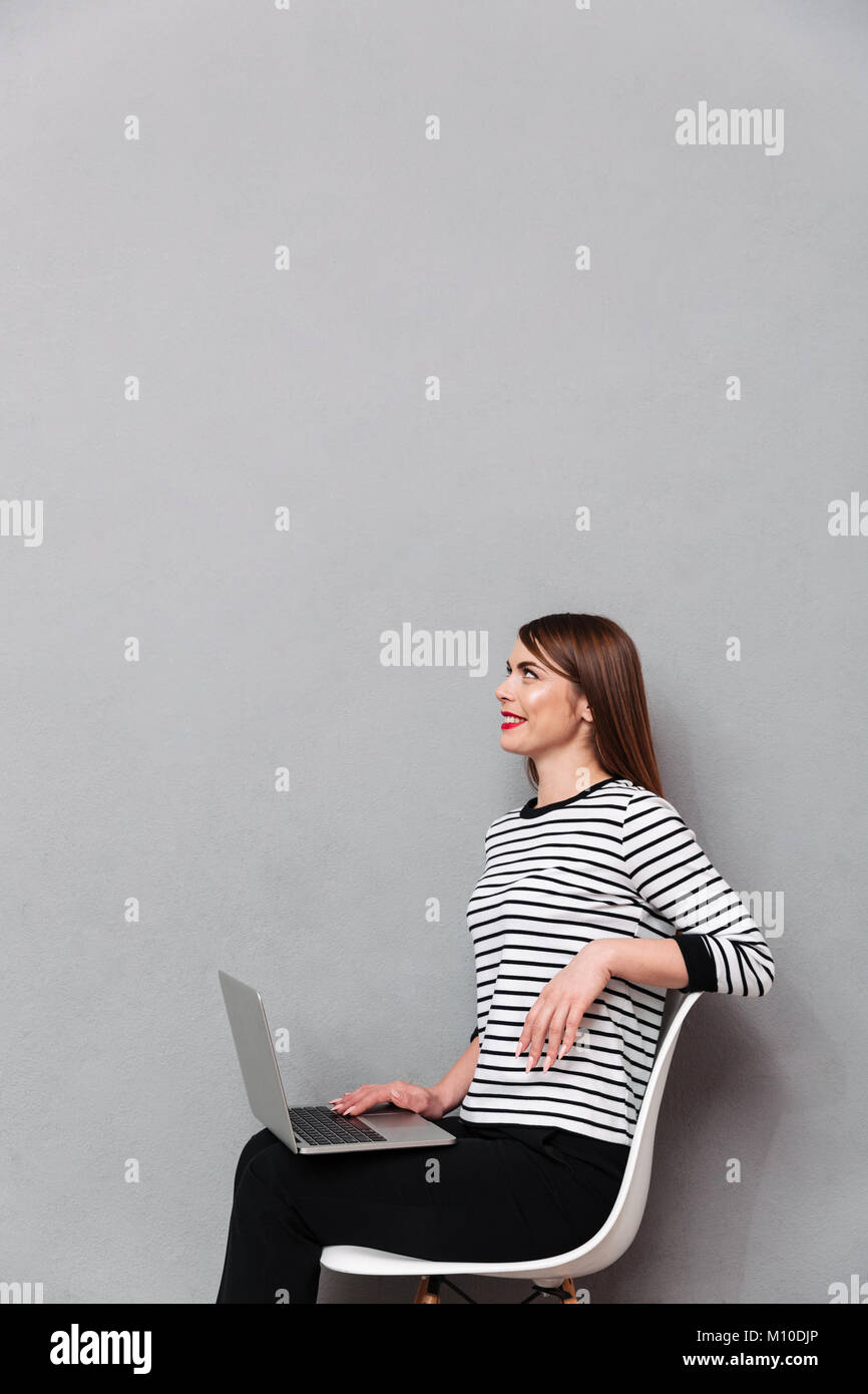 Portrait of a smiling woman sitting on chair with laptop computer and ...