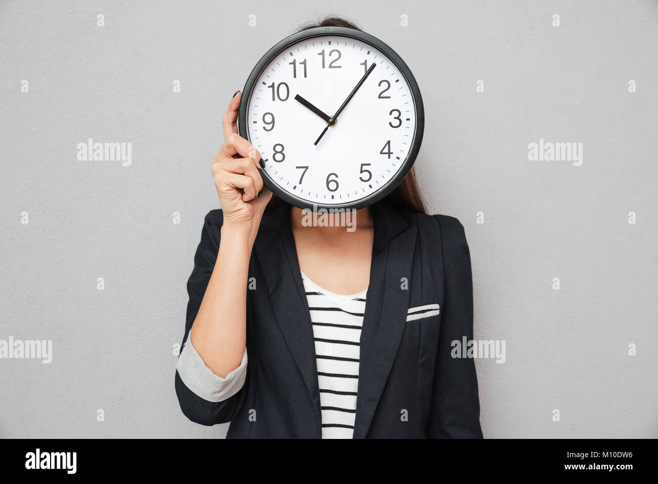 Image of Asian business woman hiding behind a clock over gray ...