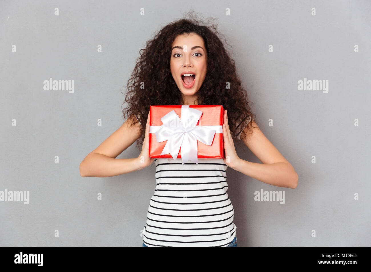 Pleased female 20s holding red box gift-wrapped, being excited and ...