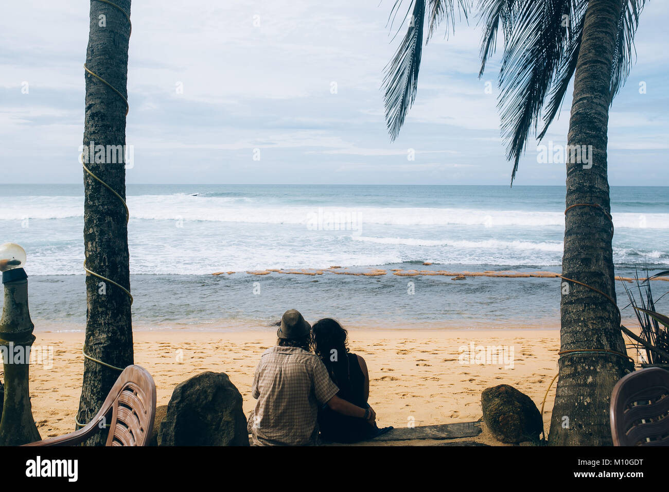 couple sitting under palm trees Stock Photo - Alamy