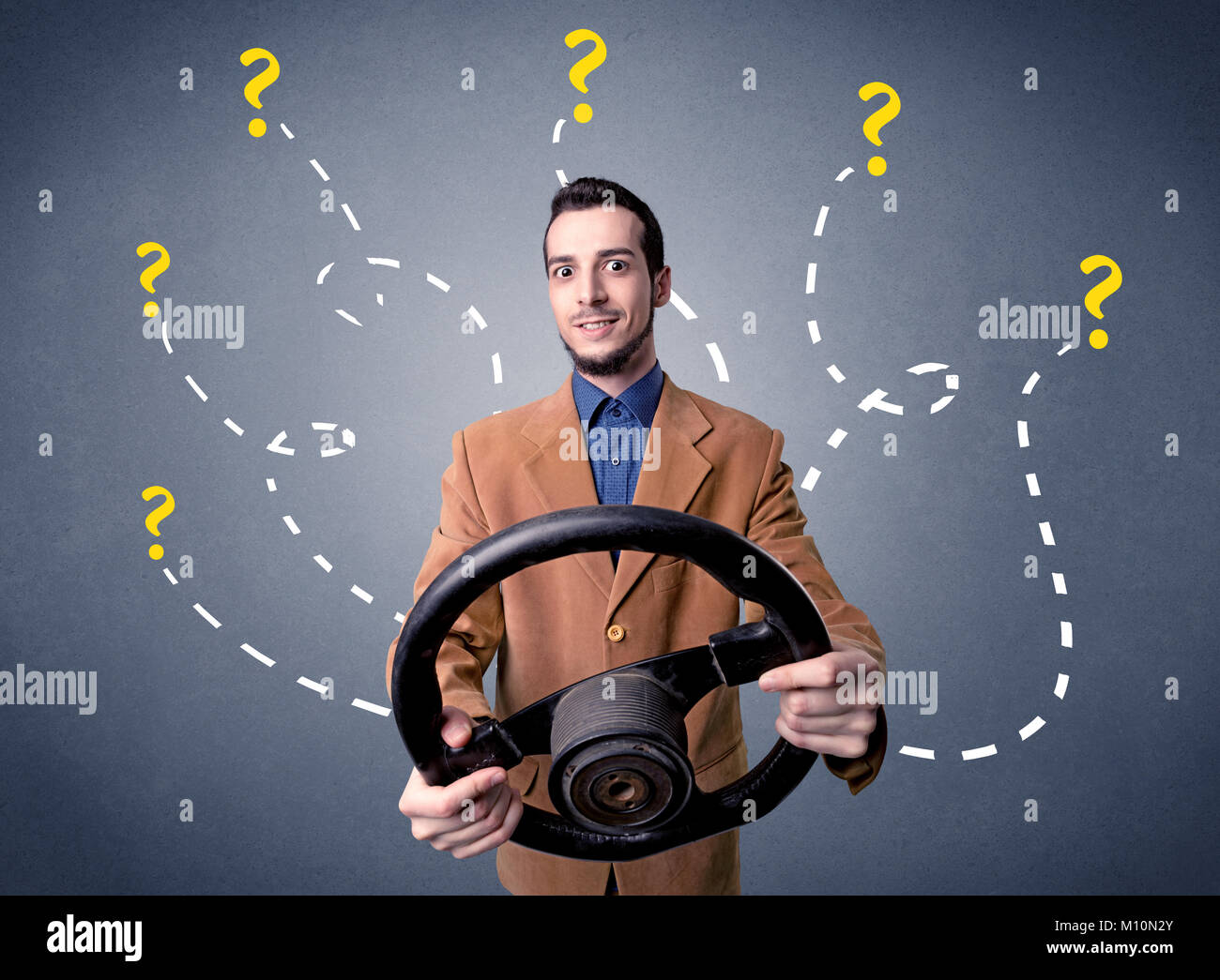 Young man holding black steering wheel with question marks around him ...