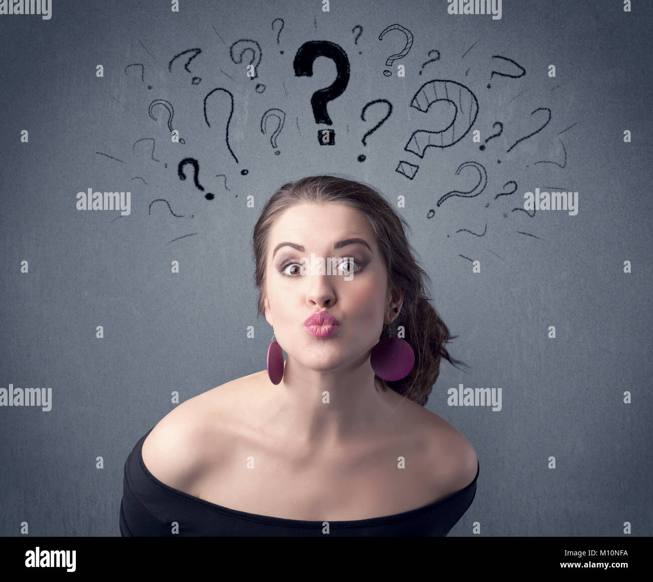 A pretty teenage girl standing confused in front of grey wall background with drawn question ...