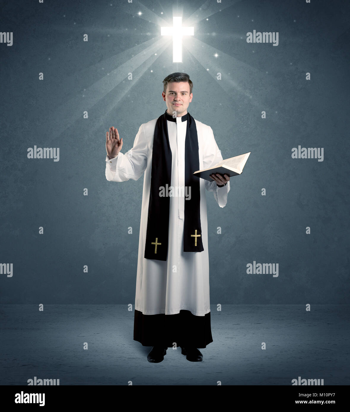 A young caucasian priest with deep faith blessing with the holy bible ...