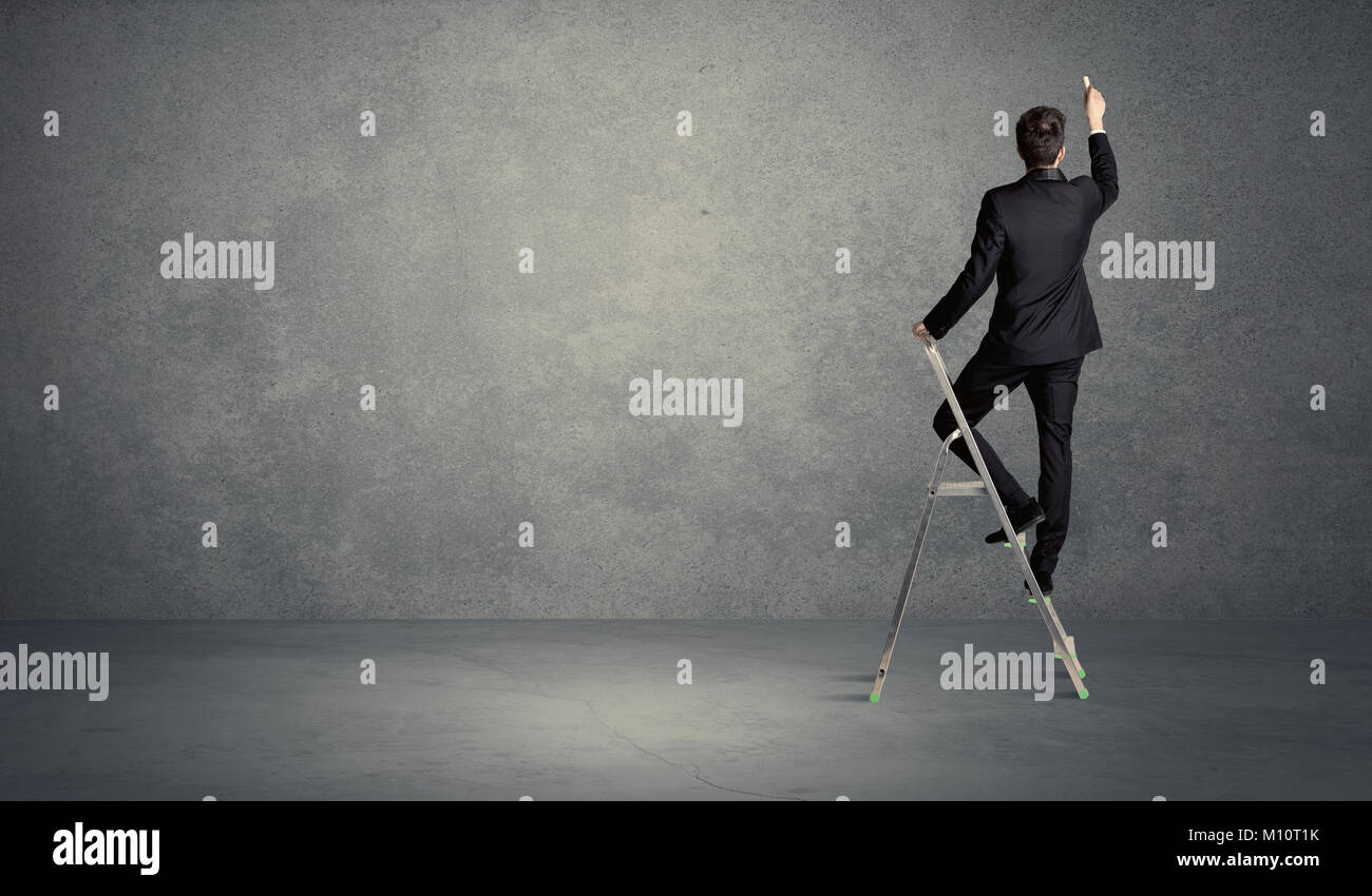 A man standing on ladder drawing with chalk in his hand on clear wall ...