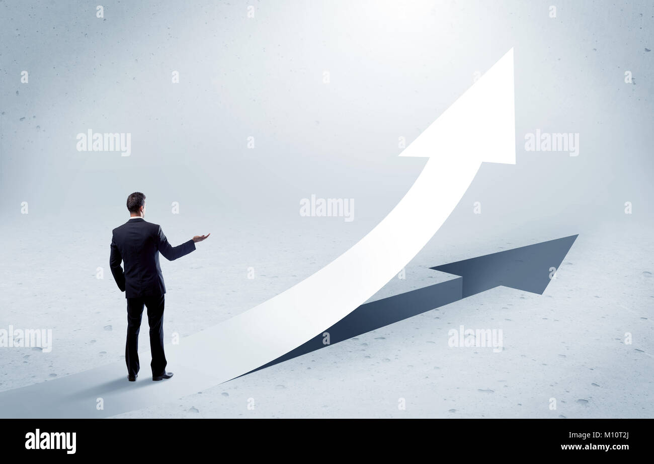 A young adult salesman standing in front of a big arrow pointing up ...