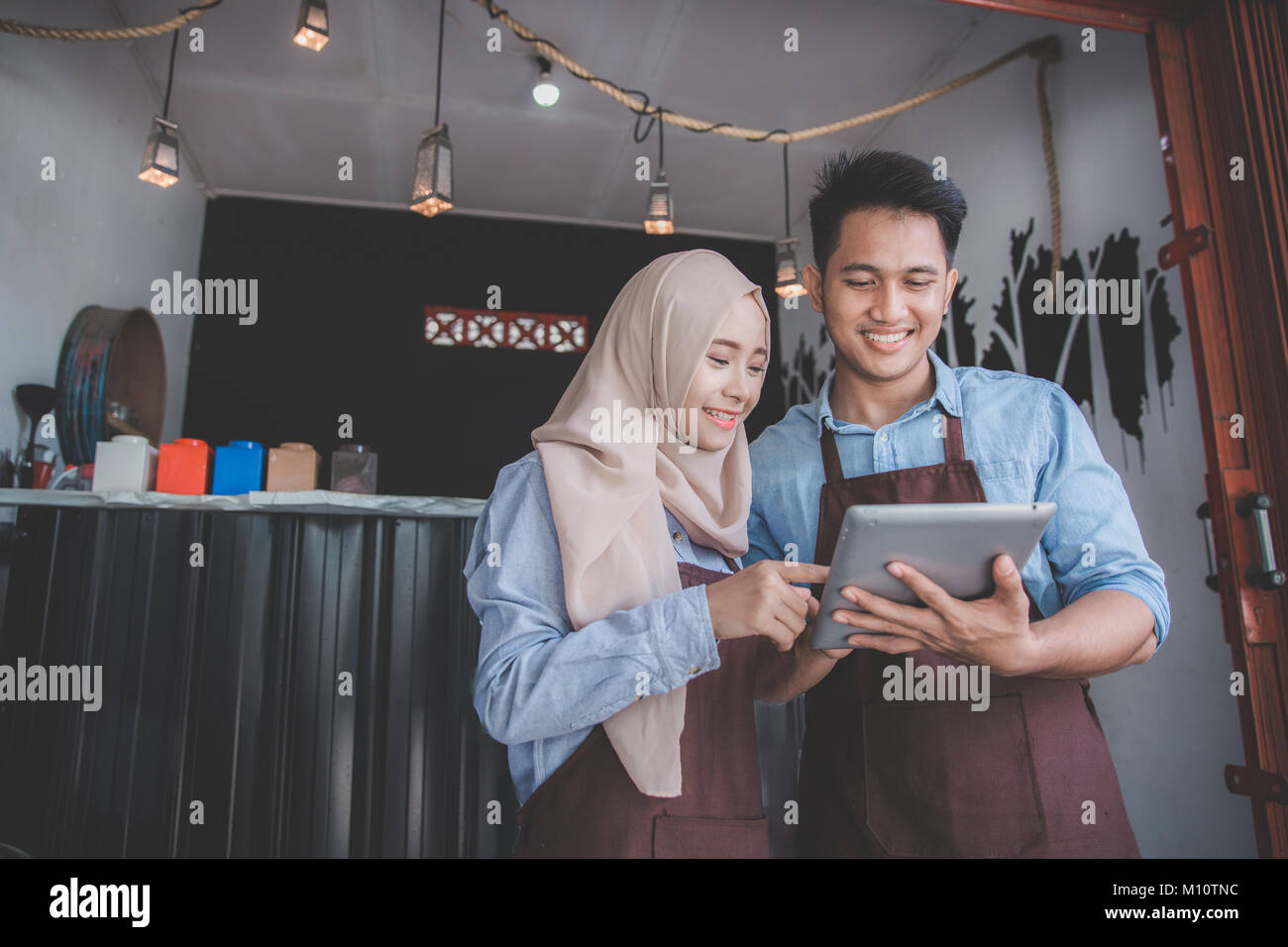 two business partner using tablet in front of their coffee shop. muslim ...
