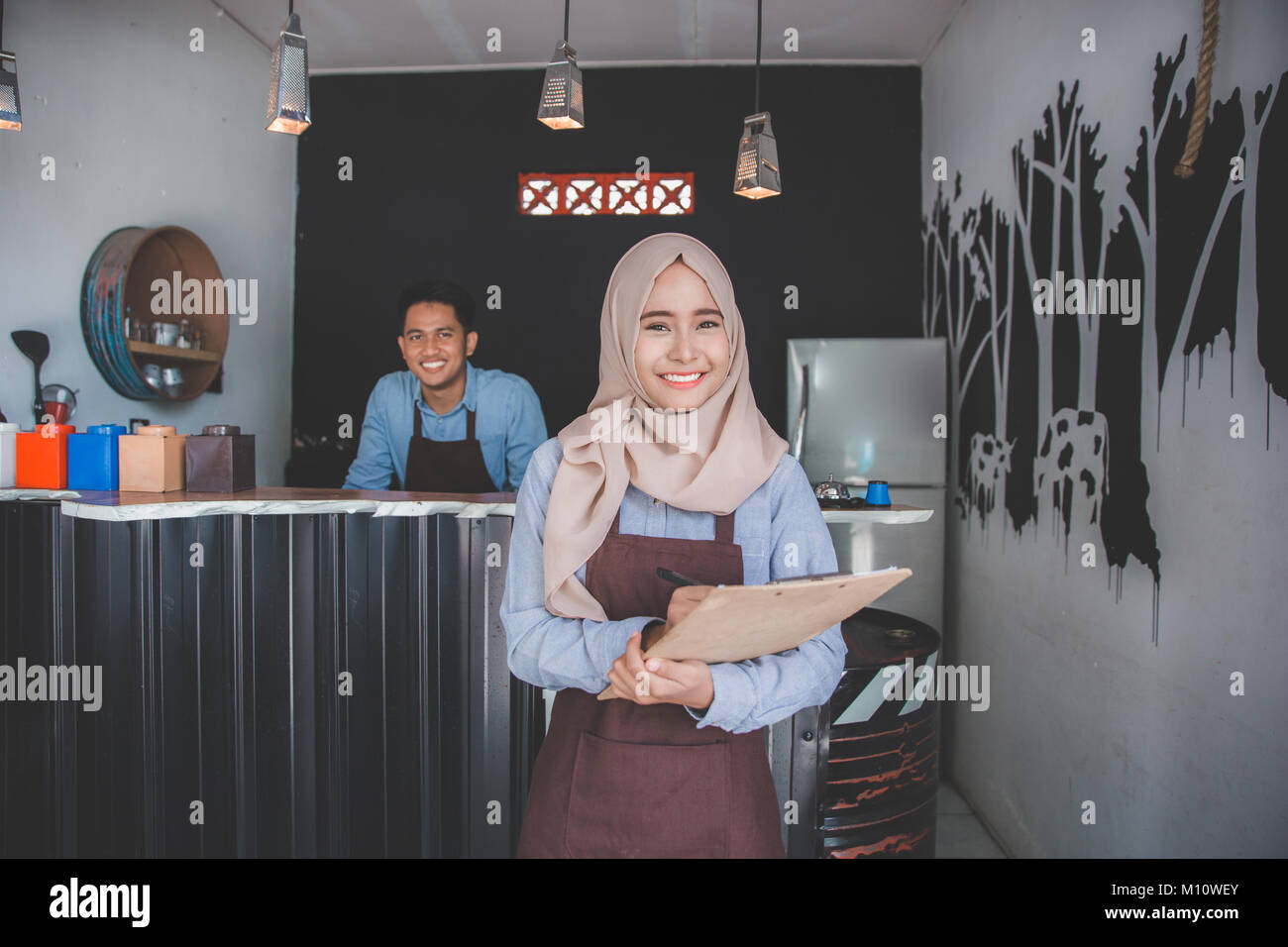 Happy asian male waiter using apron writing order. muslim entrepreneur ...